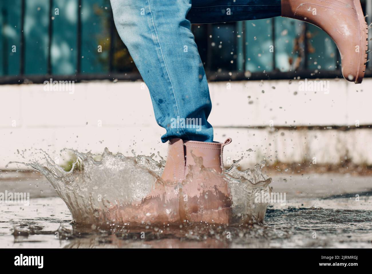 Woman wearing rain rubber boots walking running and jumping into puddle ...