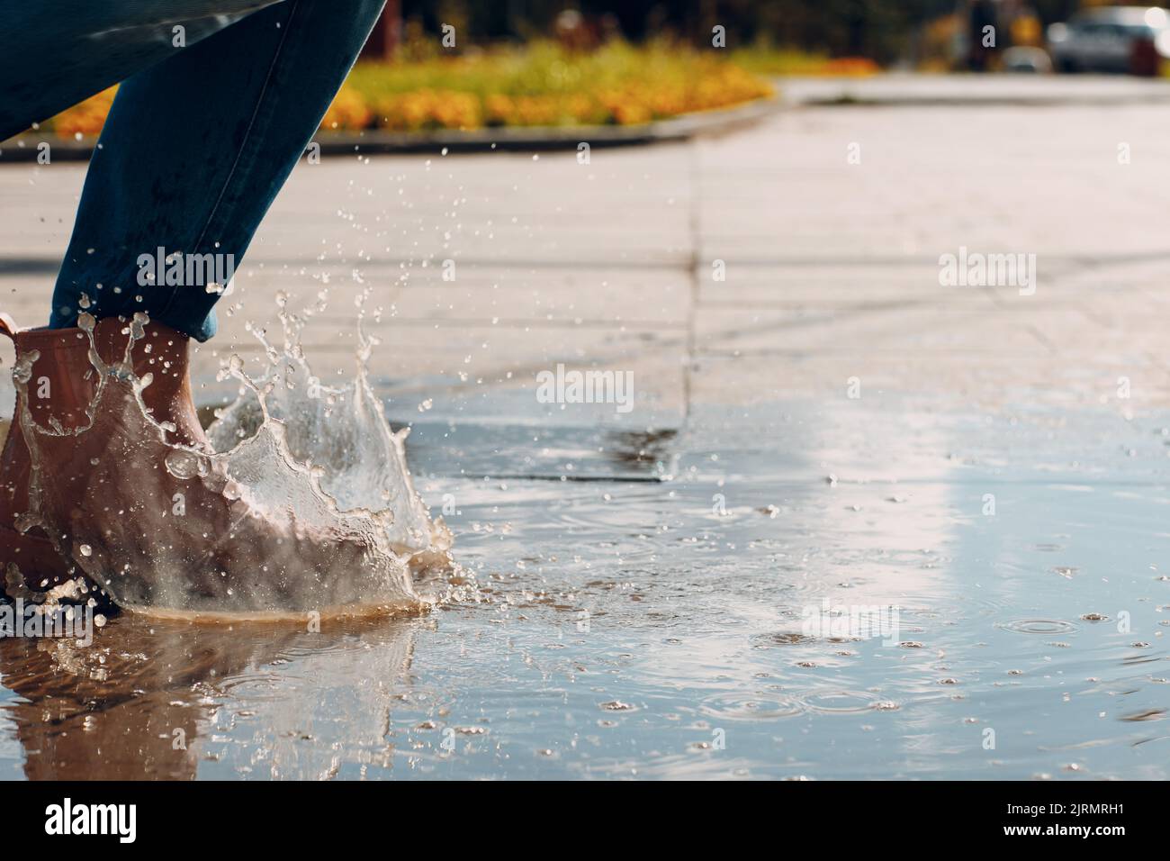 Woman wearing rain rubber boots walking running and jumping into puddle with water splash and ...