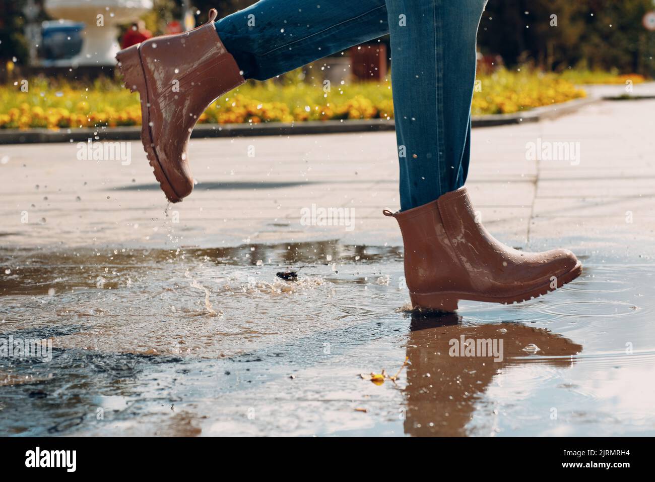 Woman wearing rain rubber boots walking running and jumping into puddle with water splash and ...