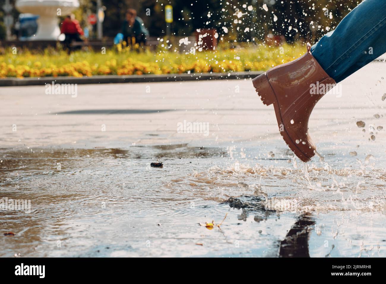 Woman wearing rain rubber boots walking running and jumping into puddle with water splash and ...