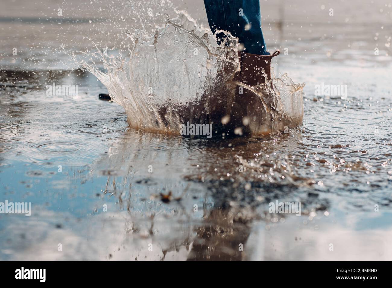 Woman wearing rain rubber boots walking running and jumping into puddle with water splash and ...