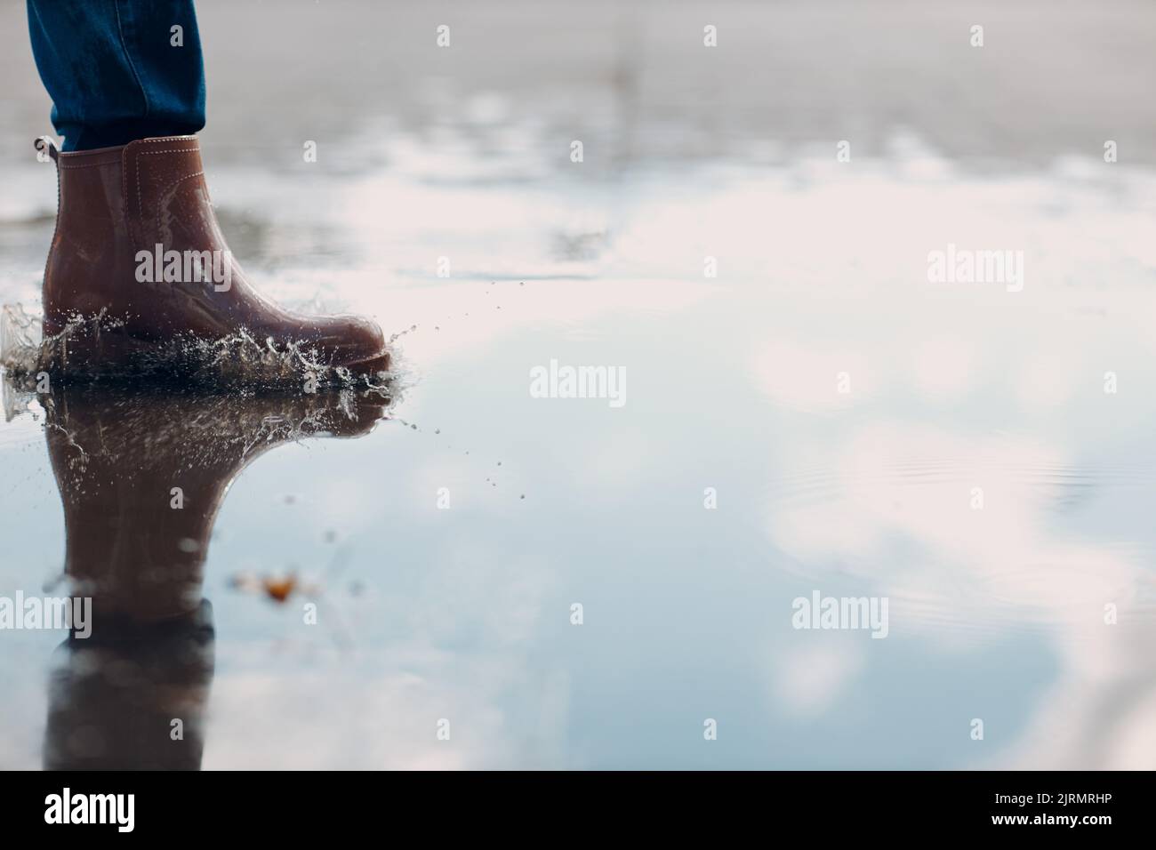Woman wearing rain rubber boots walking running and jumping into puddle ...