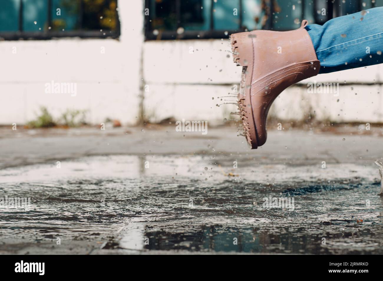 Woman wearing rain rubber boots walking running and jumping into puddle ...
