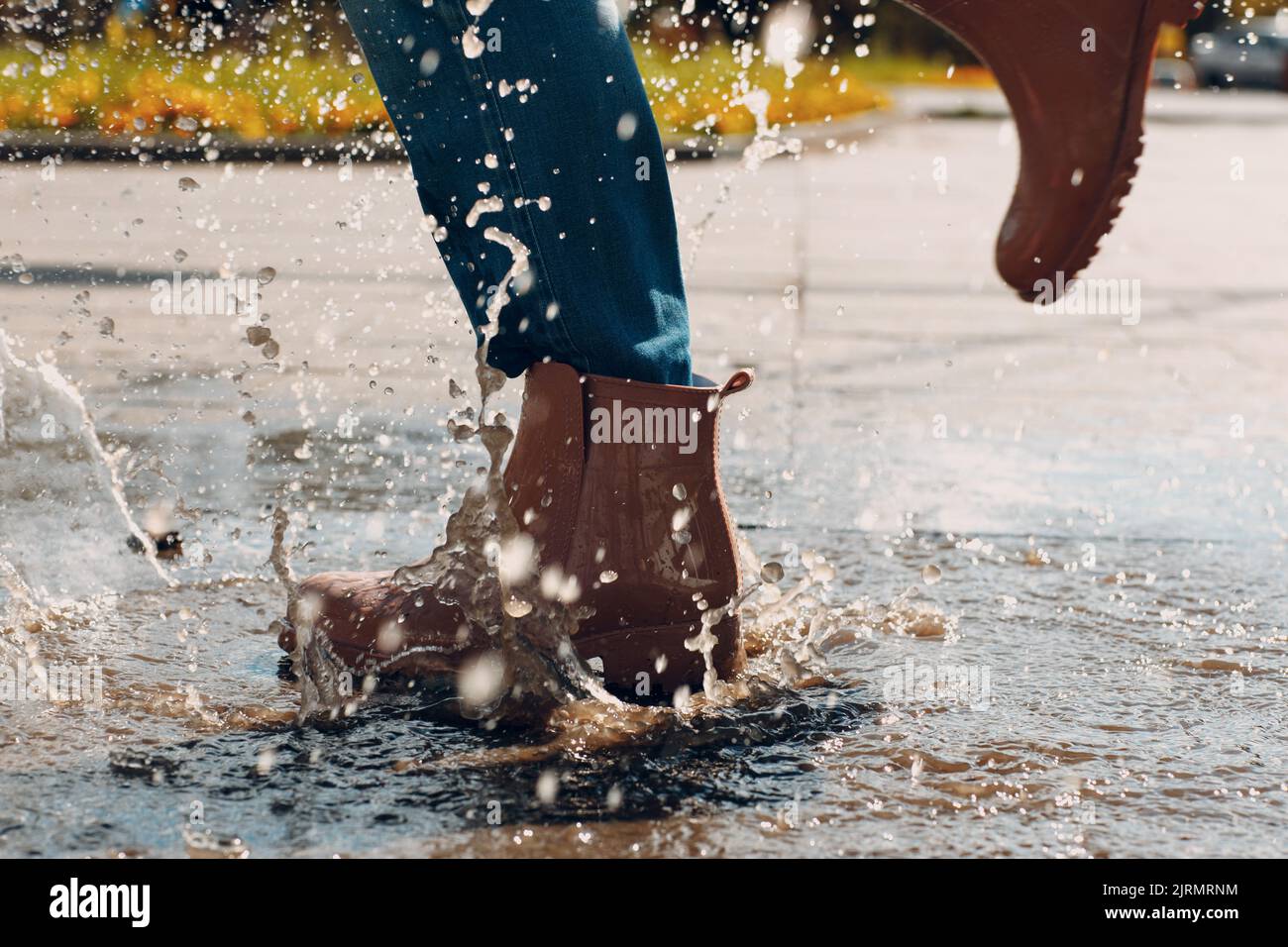 Woman wearing rain rubber boots walking running and jumping into puddle with water splash and ...