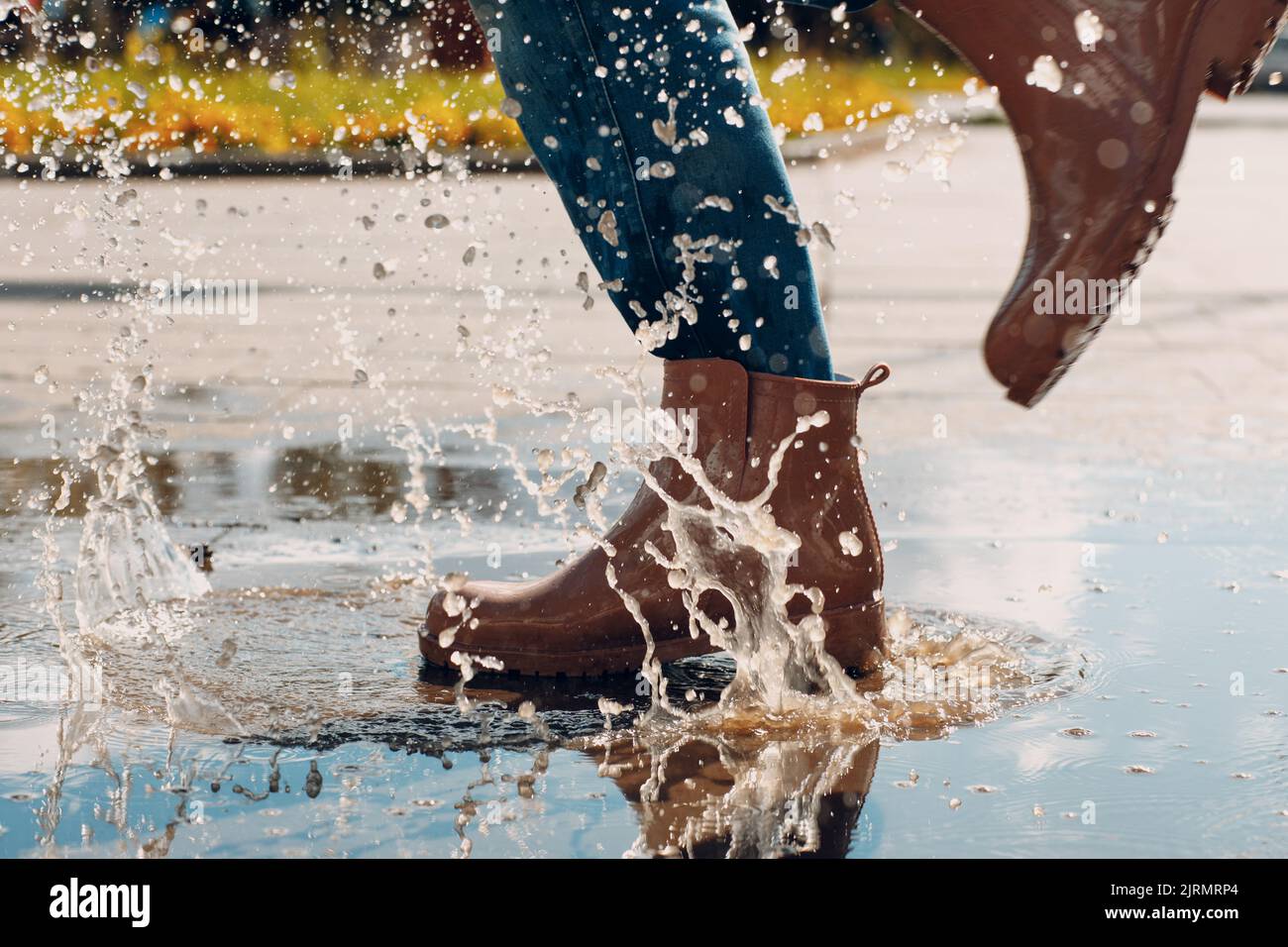 Woman wearing rain rubber boots walking running and jumping into puddle with water splash and ...