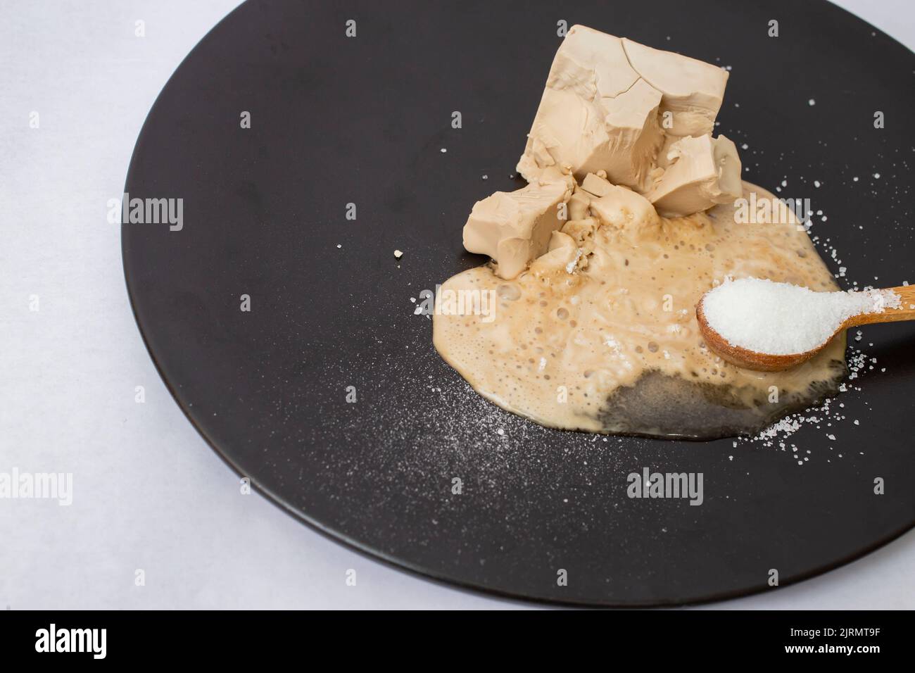 Dissolving fresh yeast with sugar on a black plate. Close up side view ...