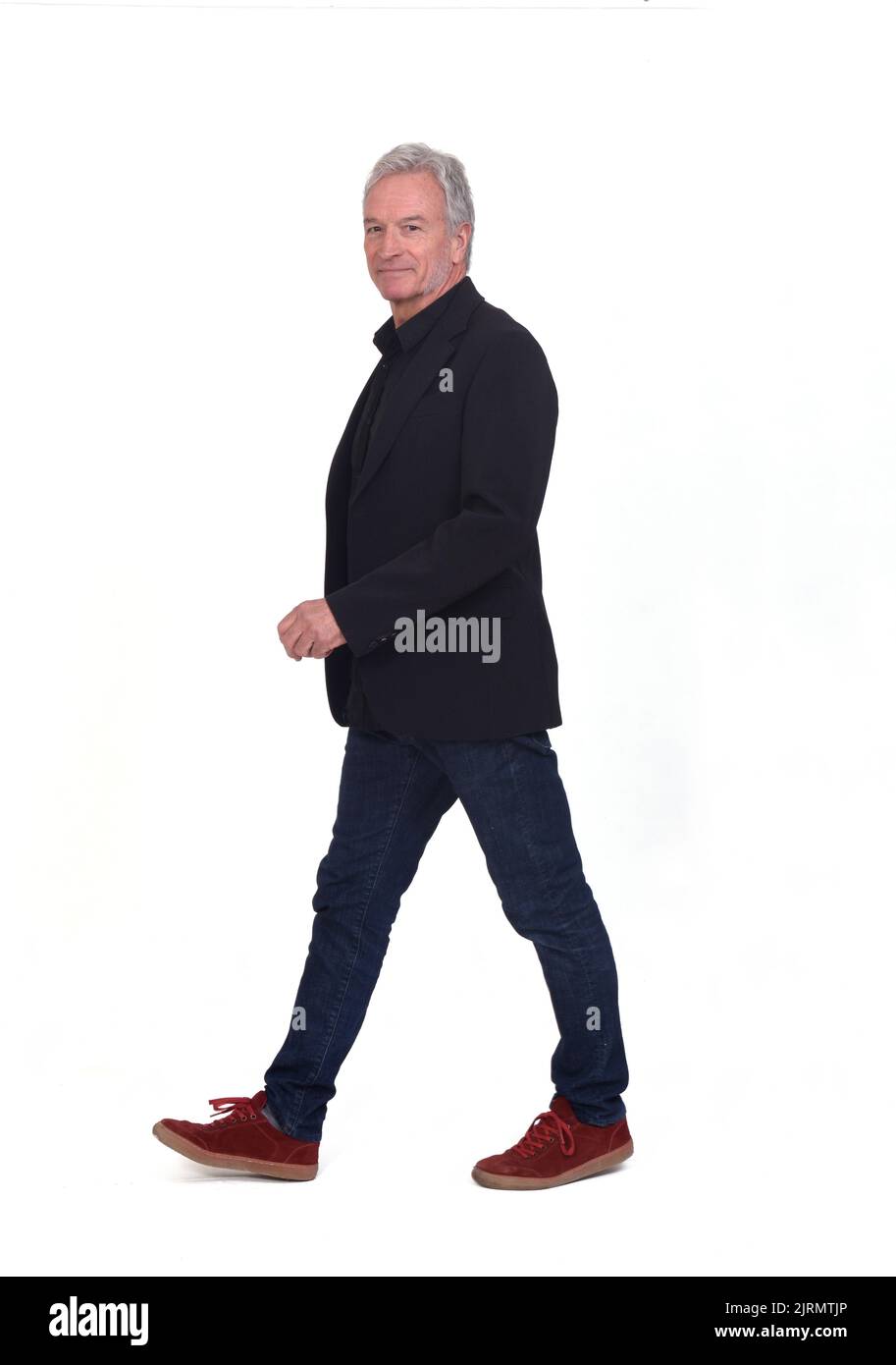 side view of senior man walking and looking at camera on white ...