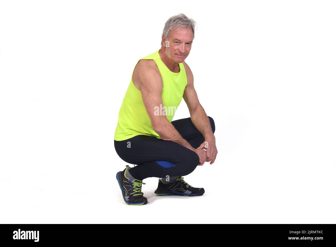side view of a senior man with sportswear squatting looking at camera ...