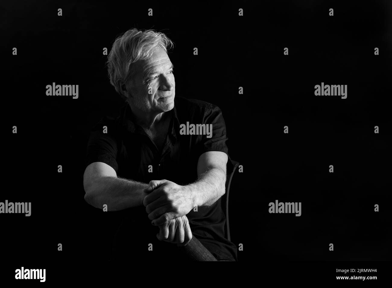 low key portrait of a senior man sitting a chair looking at away on ...