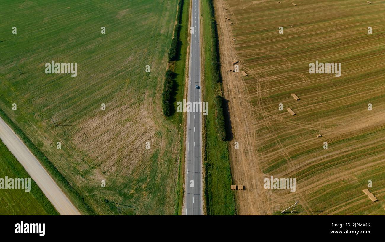 Aerial view of straight road with car between agricultural fields. View ...