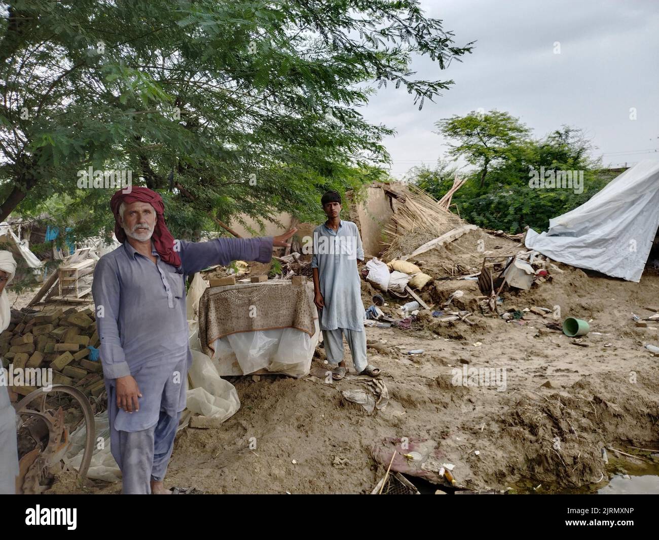 Rajanpur. 25th Aug, 2022. People stand outside damaged houses in a ...