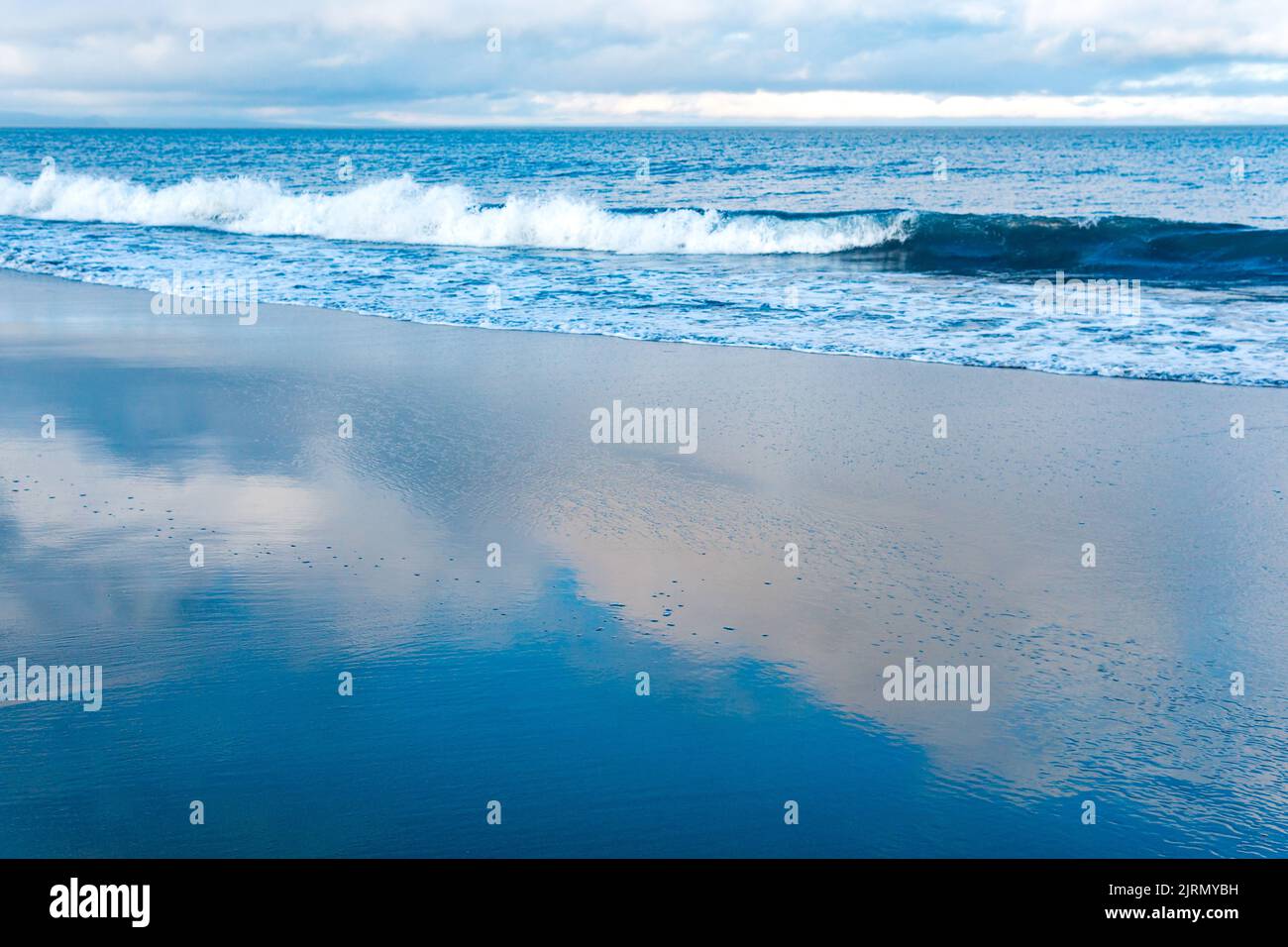 ocean beach with a wave coming back, in which the sky is reflected ...