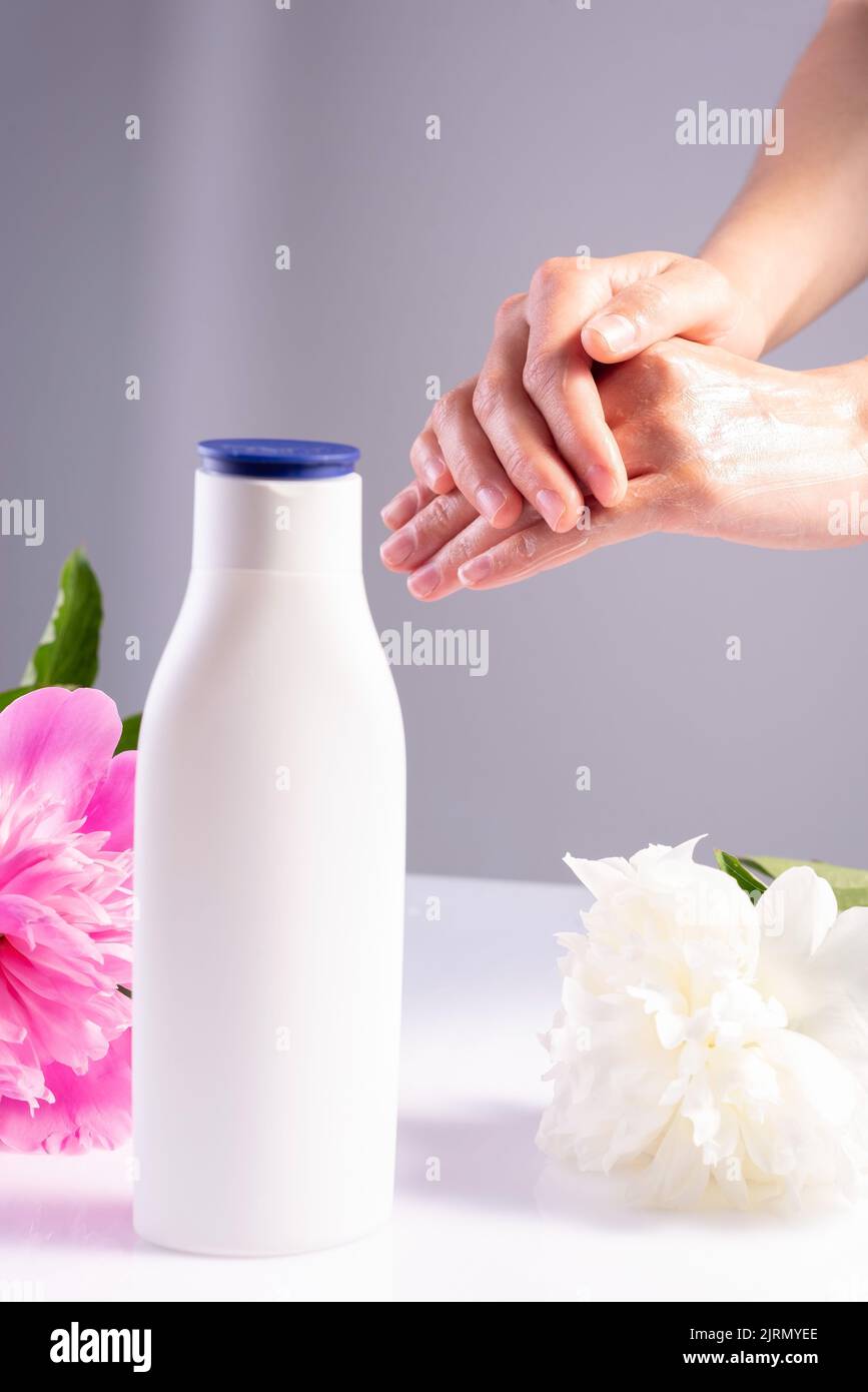 hands of the girl rubbing cream into the skin, on a white floral ...