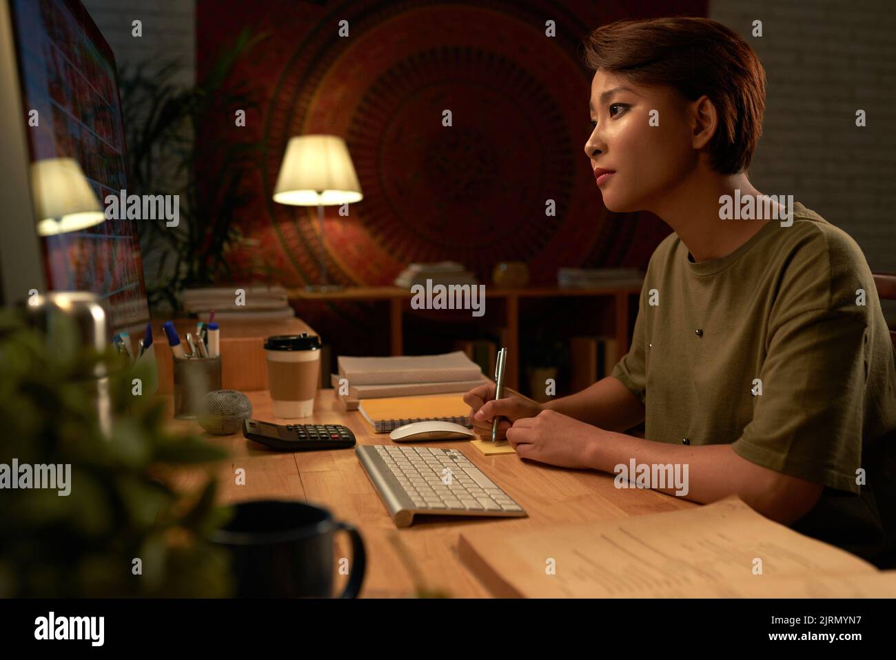 Pretty young Asian woman reading information on computer screen and ...