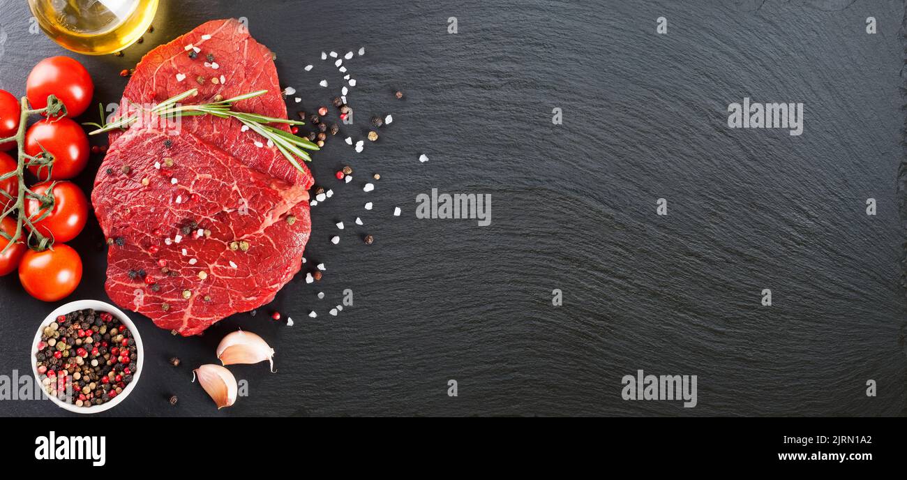 Raw beef steak with spices and ingredients for cooking on black slate ...