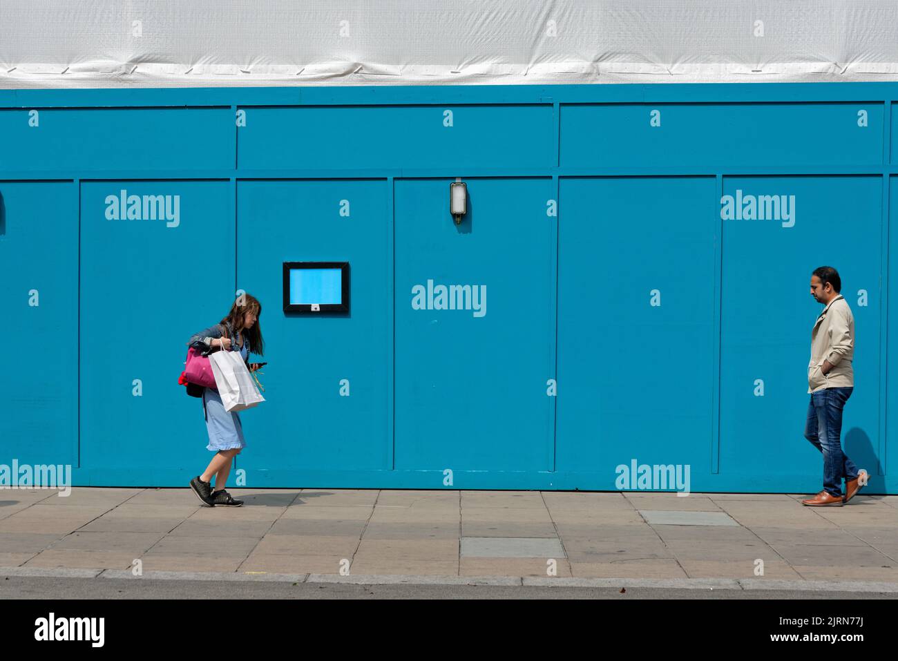 People passing by a blue building hoarding creating an abstract image ...