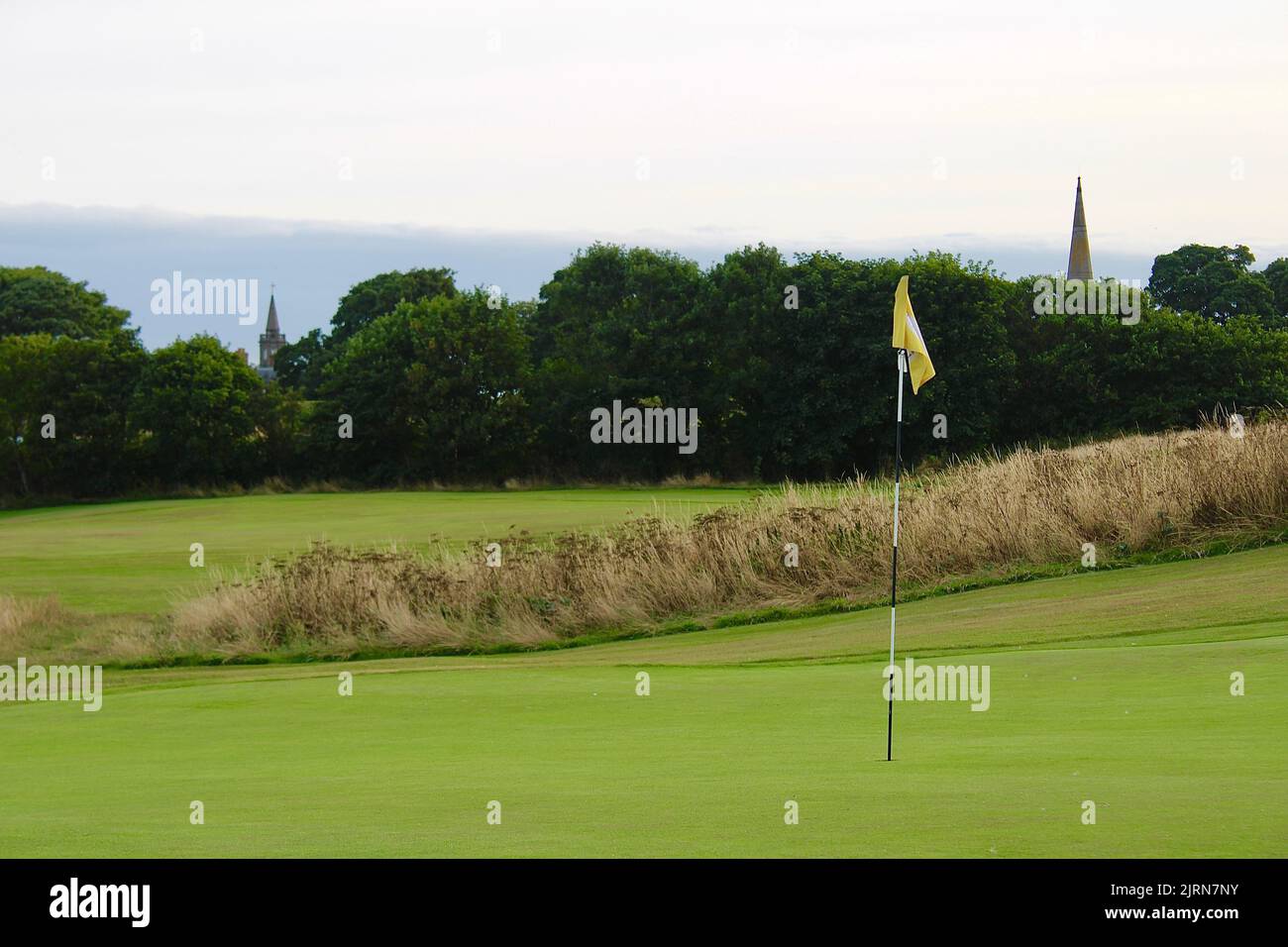 A golf course with trees and church roofs in the background Stock Photo ...