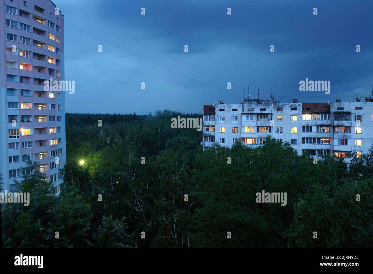 Buildings plunged in the forest lights in windows cloudy sky night view ...