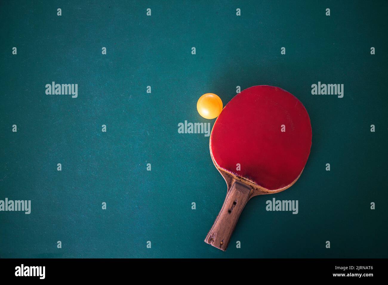 A top view of a red table tennis racket and an orange ball on a green ...
