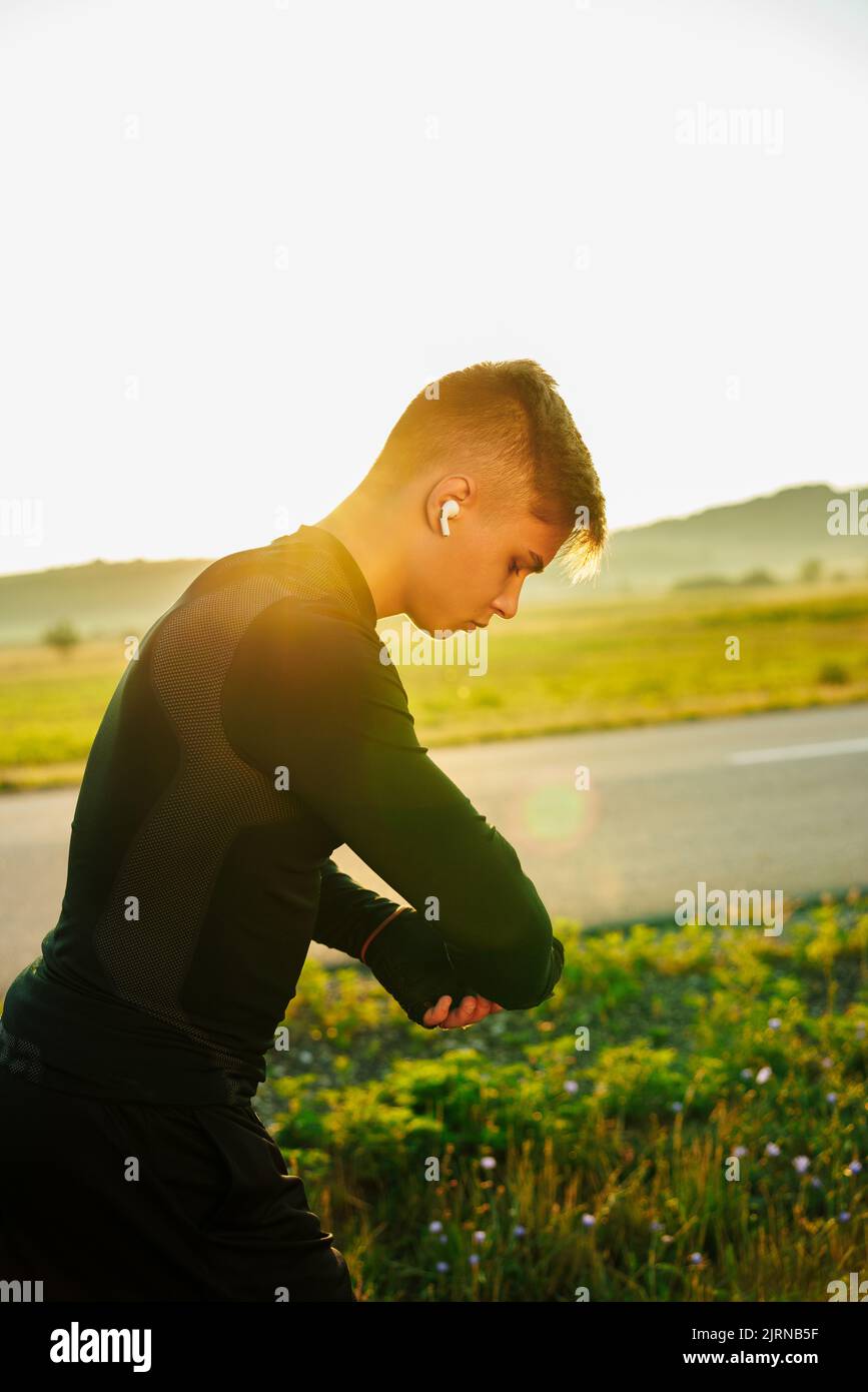 A handsome athlete looks at the smart watch on his wrist while running ...