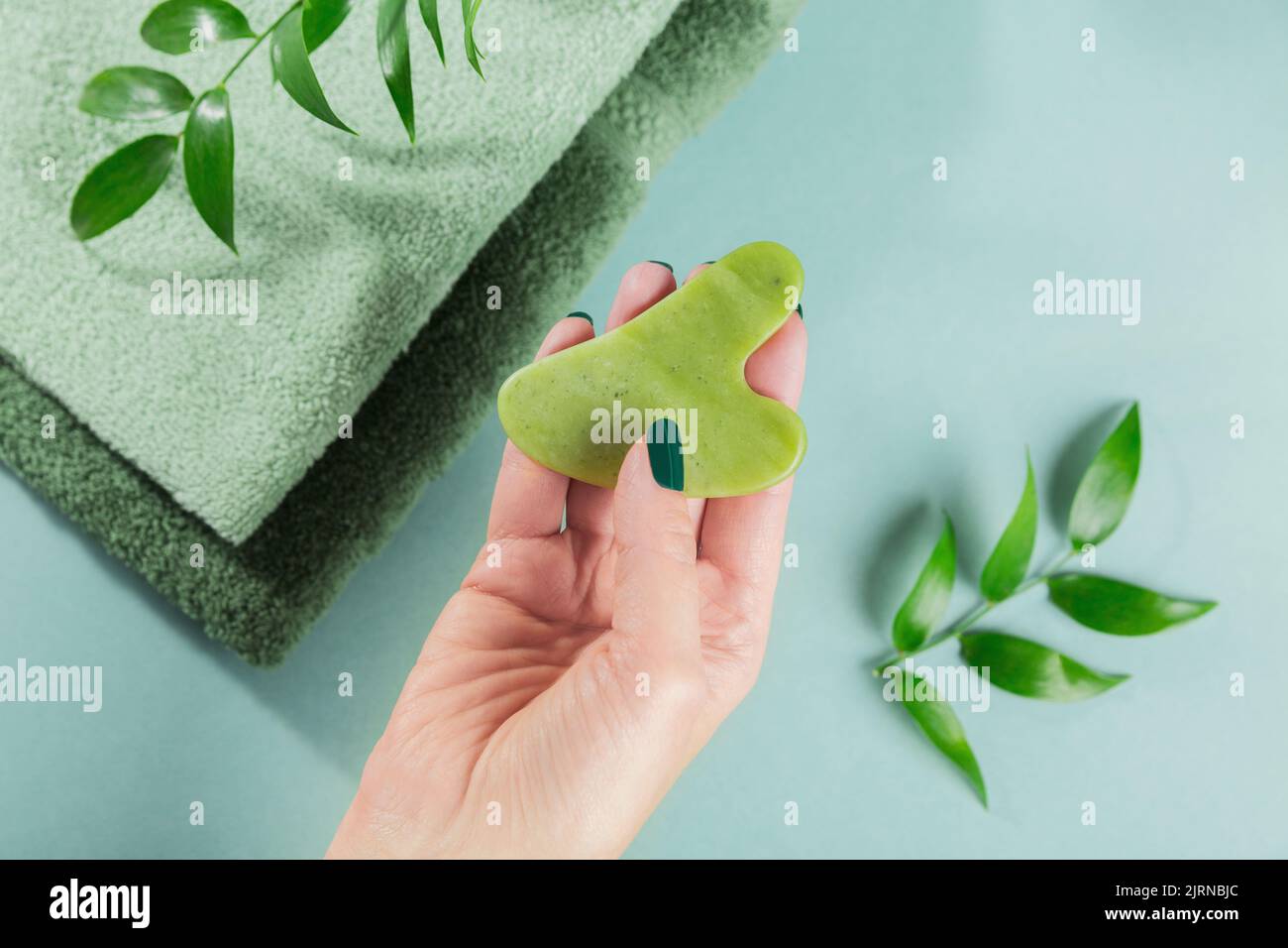 Female hand holding massage gua sha scraper for the face of green jade ...