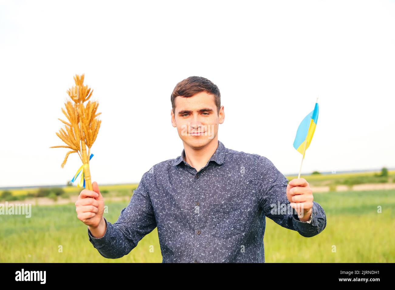 Defocus young man holding ukrainian flag and wheat spikes of wheat tied ...