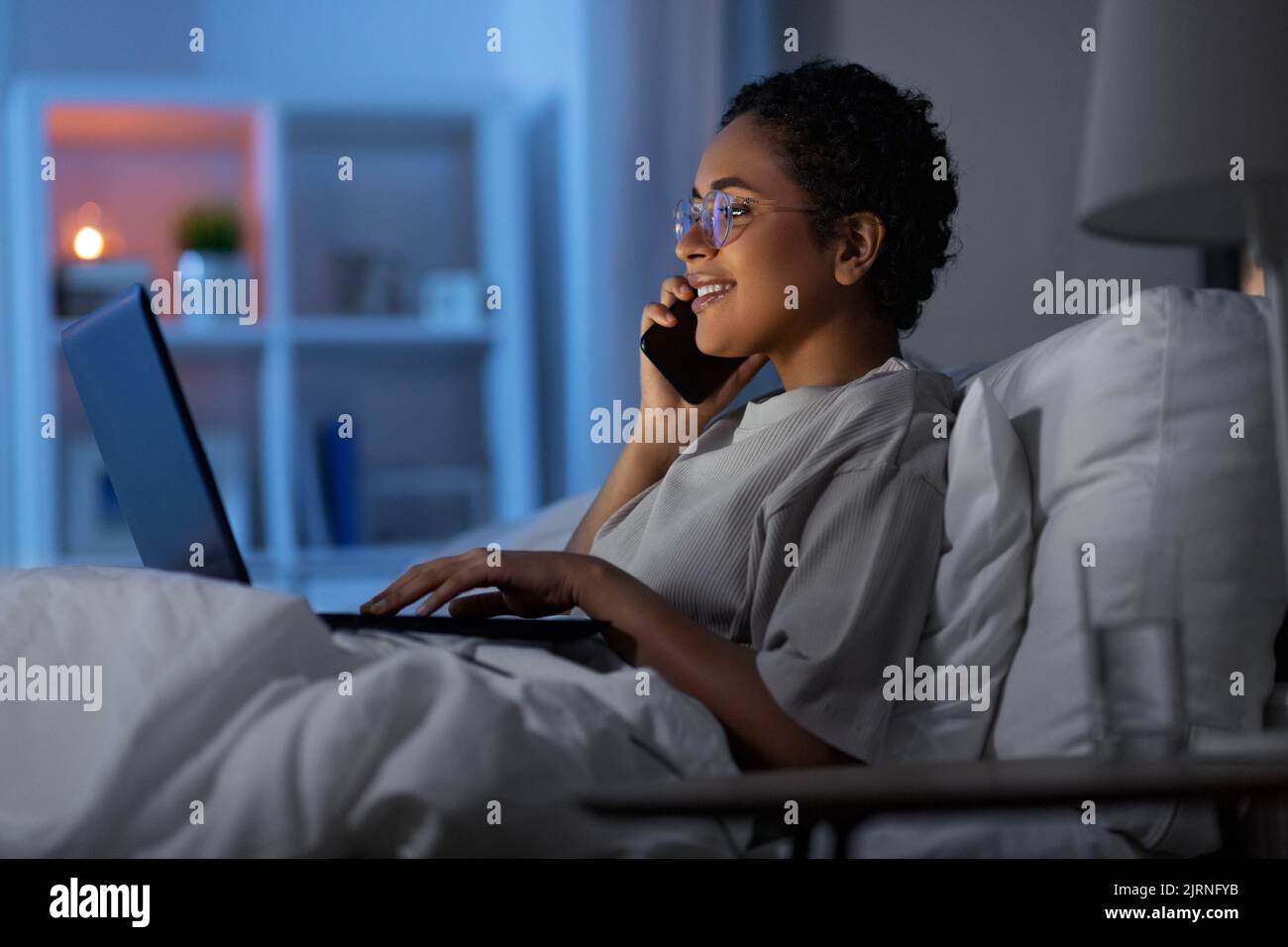 woman with laptop calling on phone in bed at night Stock Photo - Alamy