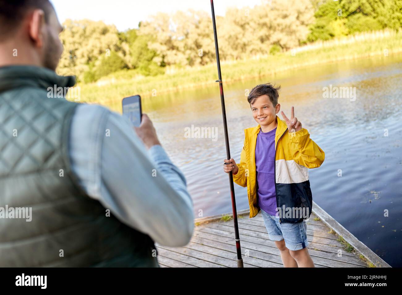 father photographing son with fishing rod on river Stock Photo - Alamy