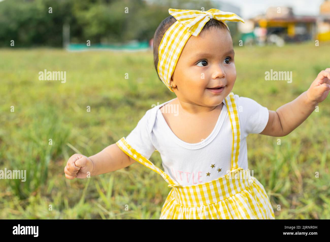 little latin girl standing in a grassy field, smiling and looking very ...