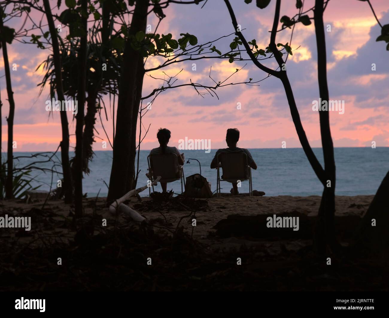 Couples sit and watch the sunset by the sea. Silhouettes of women and ...