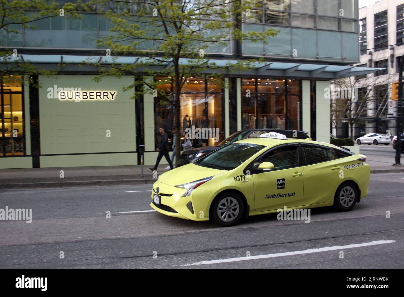 A yellow taxi driving in front of a luxury store in downtown Vancouver ...