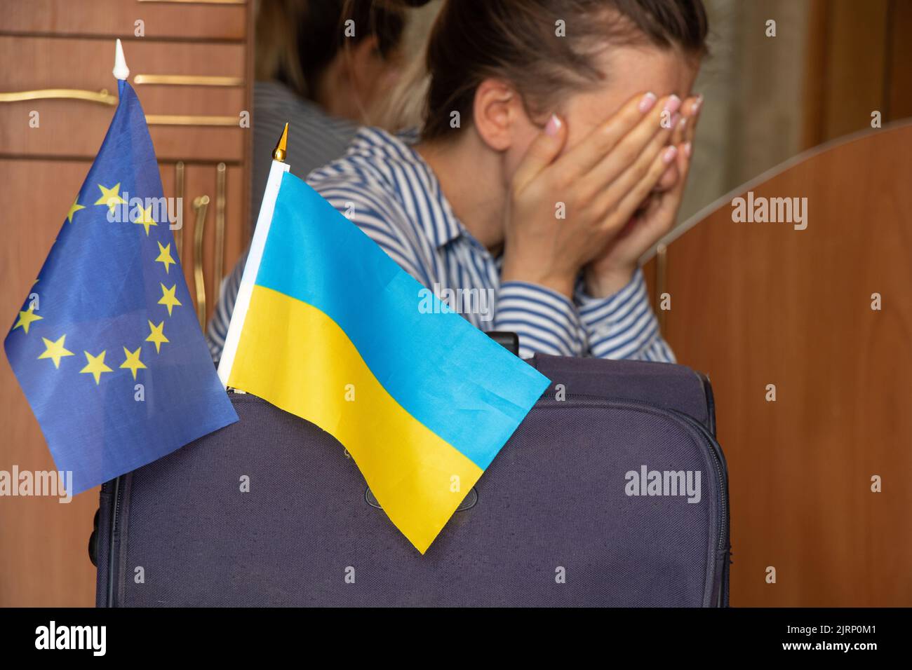 A girl is crying near a suitcase with flags of Ukraine and the flag of ...