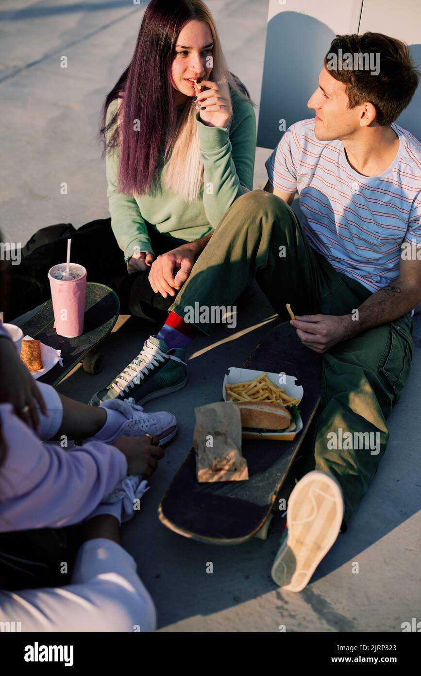 A small group of teenagers sitting outdoors and having fast food for a ...