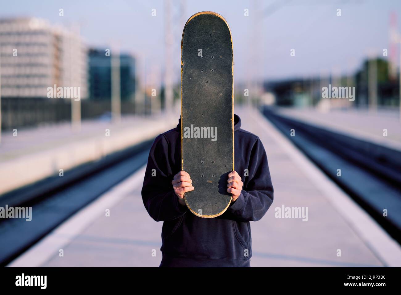 A teenage boy is standing at the train station and holding a skateboard ...