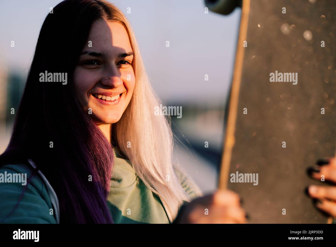 Portrait of a teenage skater girl holding skateboard towards sun and ...