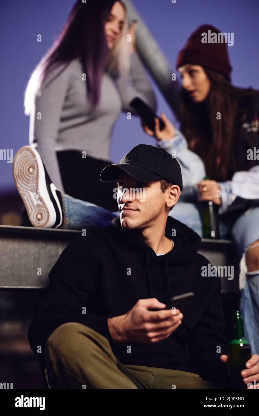 Teenage friends chilling with bottles of beer at roof party at night ...