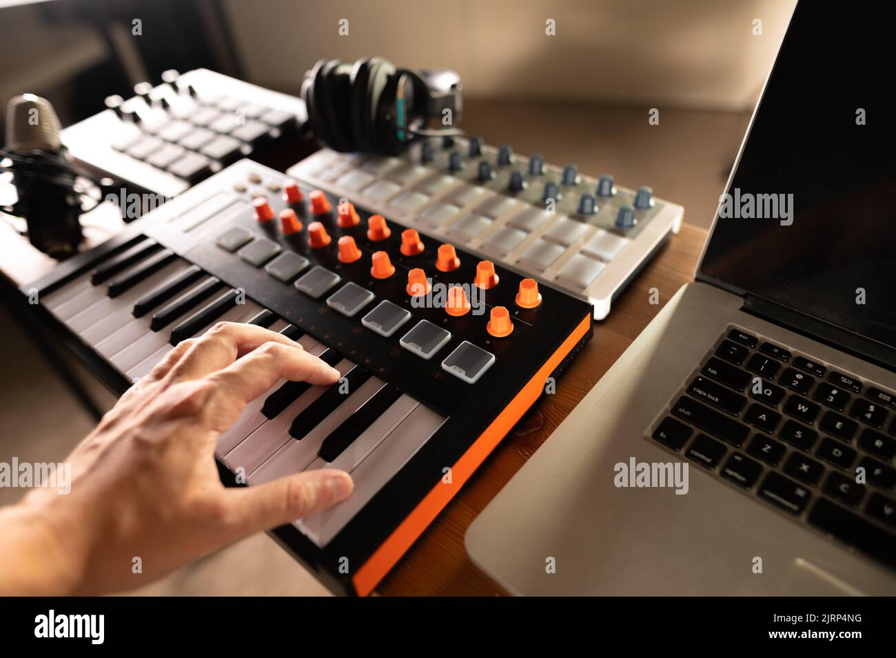 Studio headphones on a midi keyboard and a person's hand on the keys ...