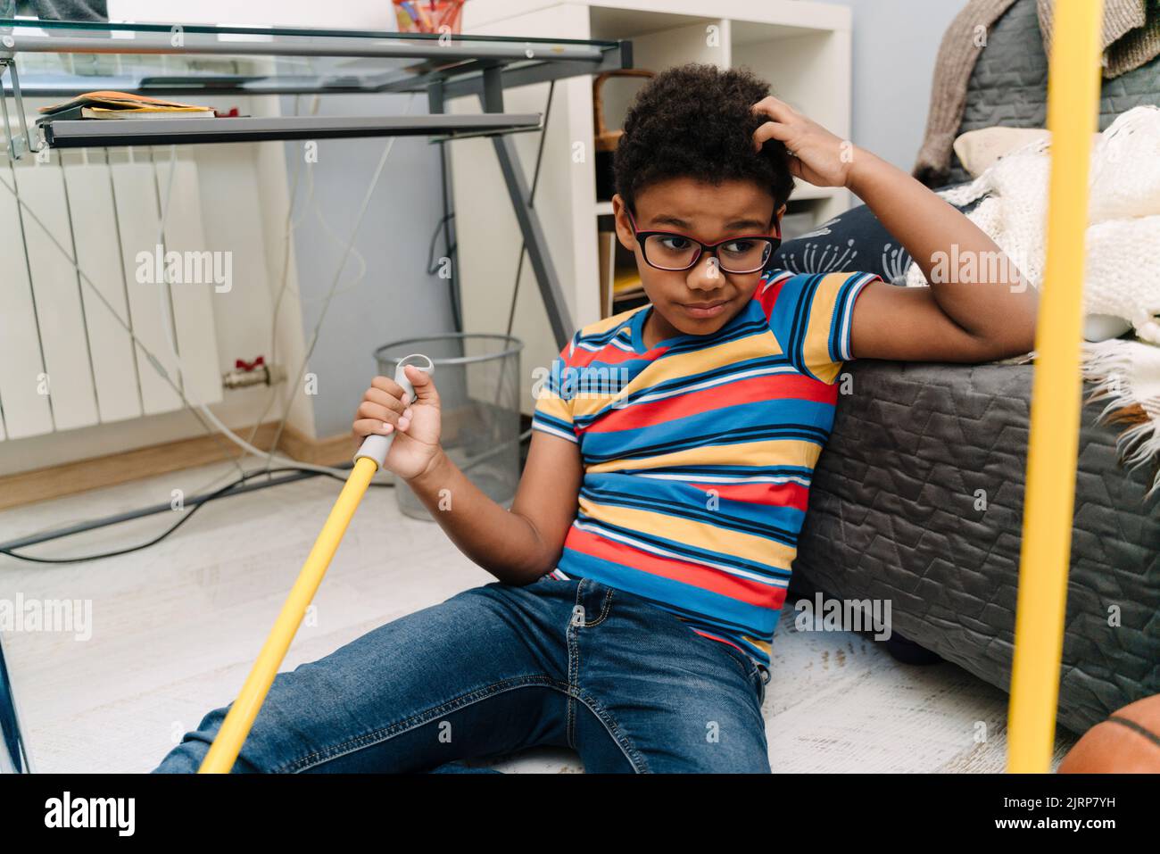 Black boy in eyeglasses sitting on floor while doing housework at his ...