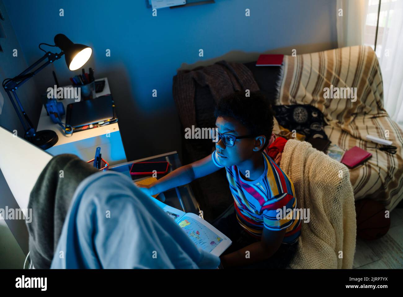 Black boy doing homework with computer while sitting at table in home ...