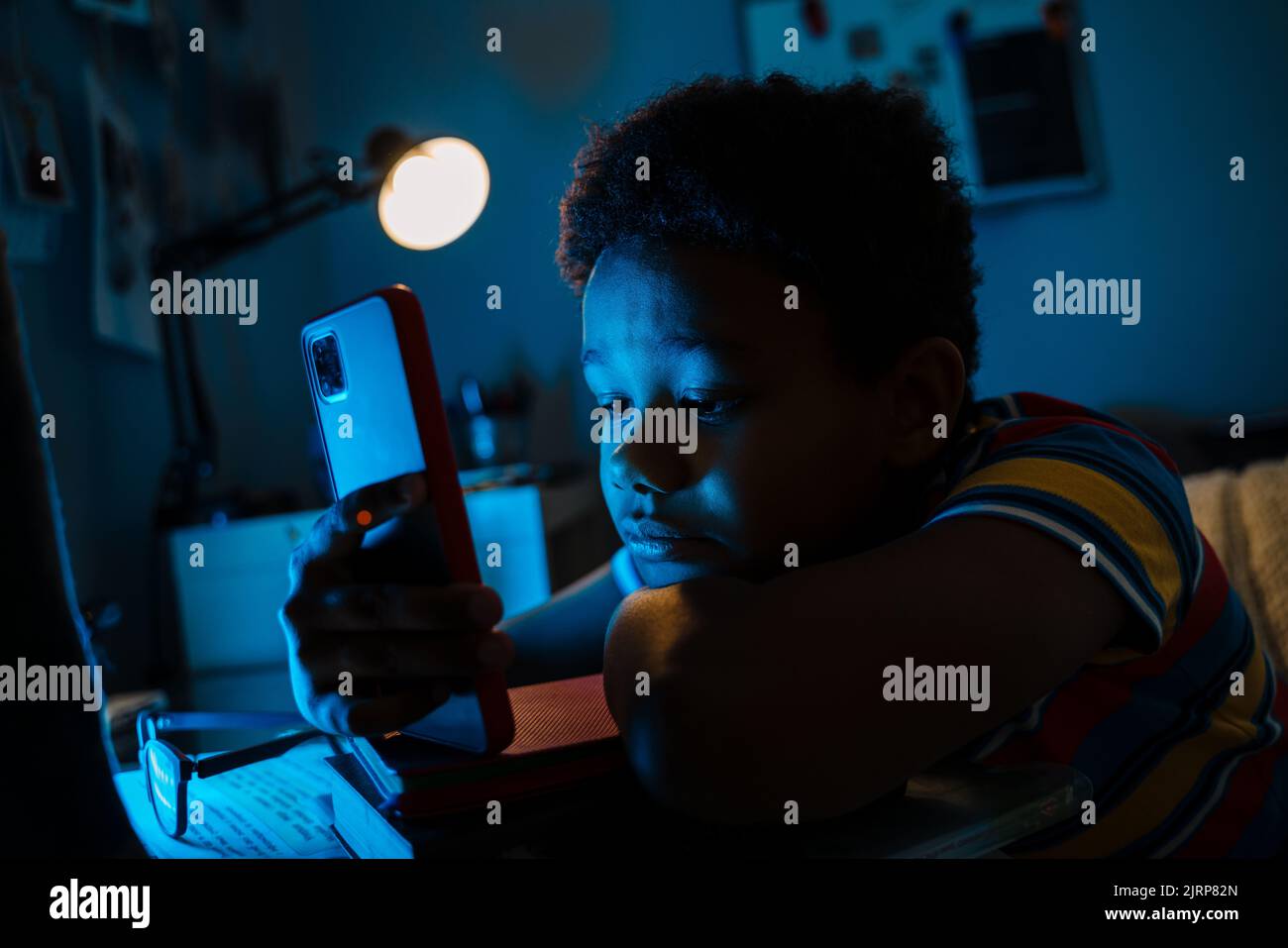Black boy using mobile phone while sitting by computer screen in home ...