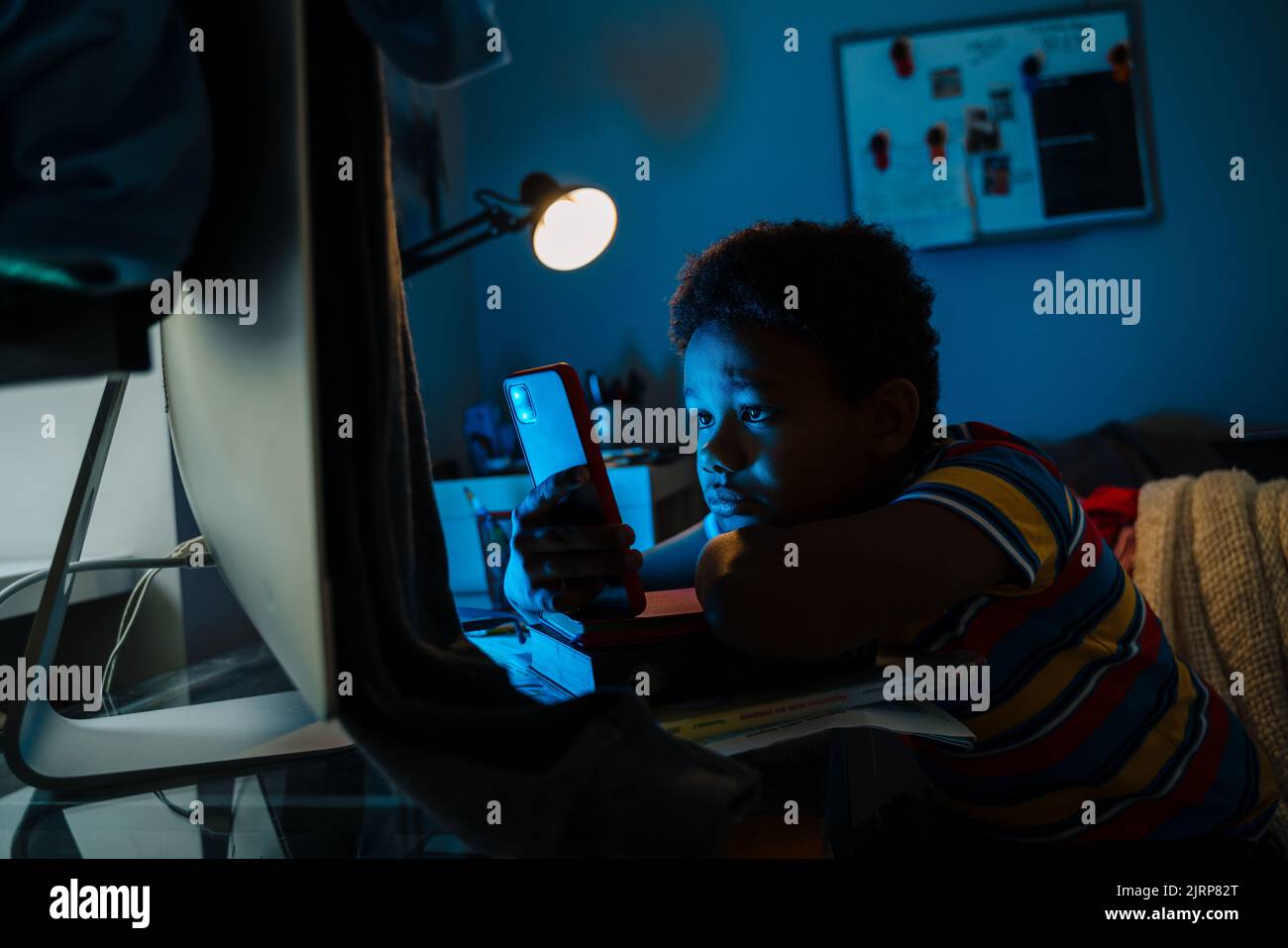 Black boy using mobile phone while sitting by computer screen in home ...