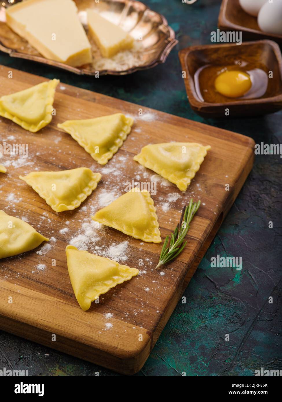 Homemade ravioli on a cutting board sprinkled with flour on a dark ...