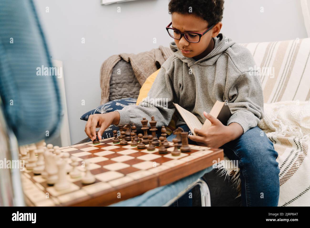 Black boy in eyeglasses playing chess while sitting on sofa at home Stock Photo - Alamy