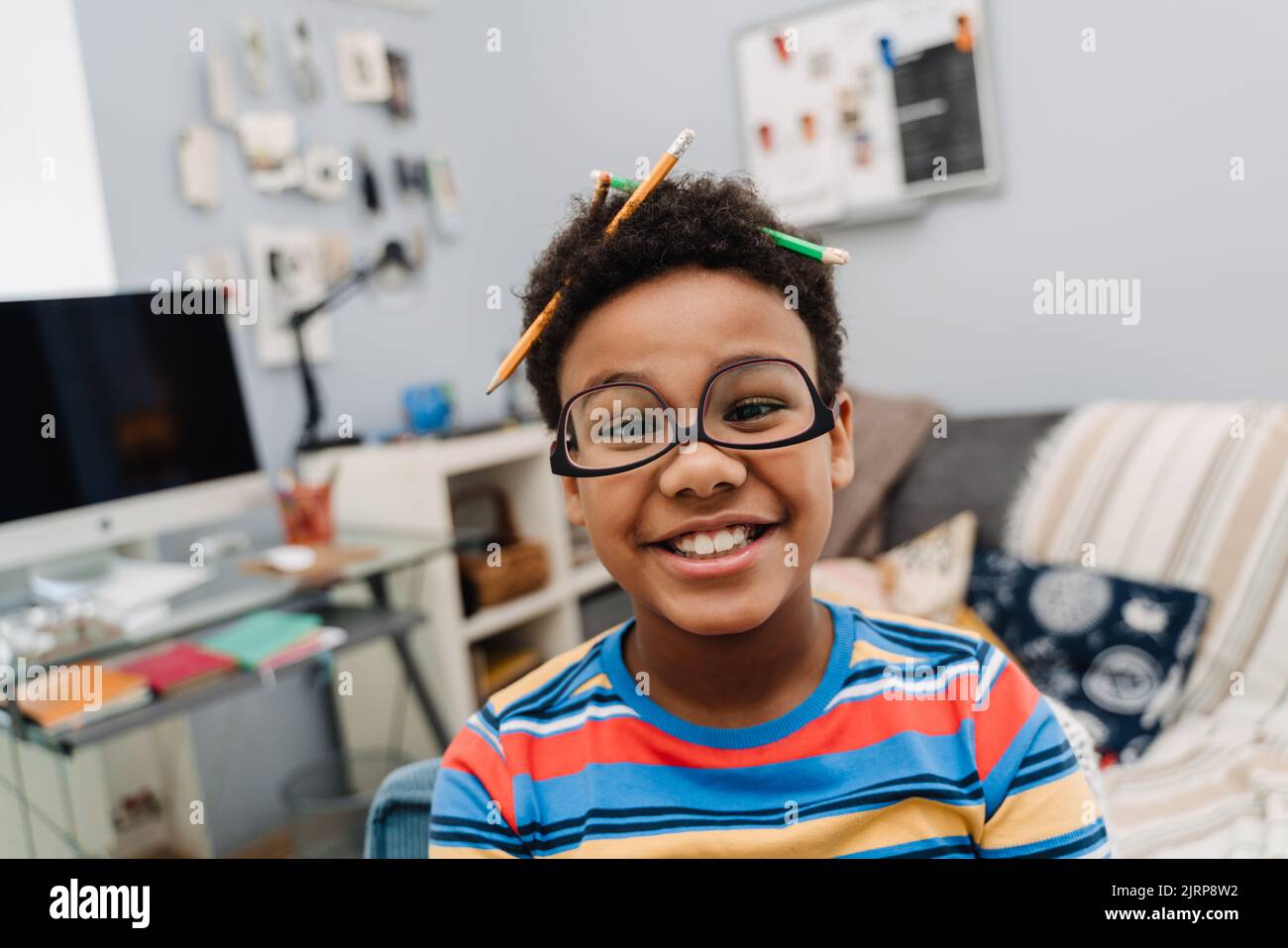 Black boy laughing while making fun with pencils and eyeglasses at home ...