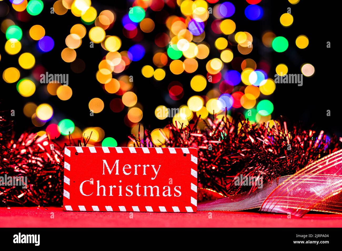 A closeup of a red Merry Christmas card with a tinsel in blurred lights ...