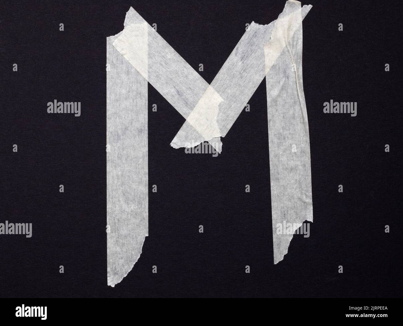 The letter M taped on a black background made from torn adhesive strips ...