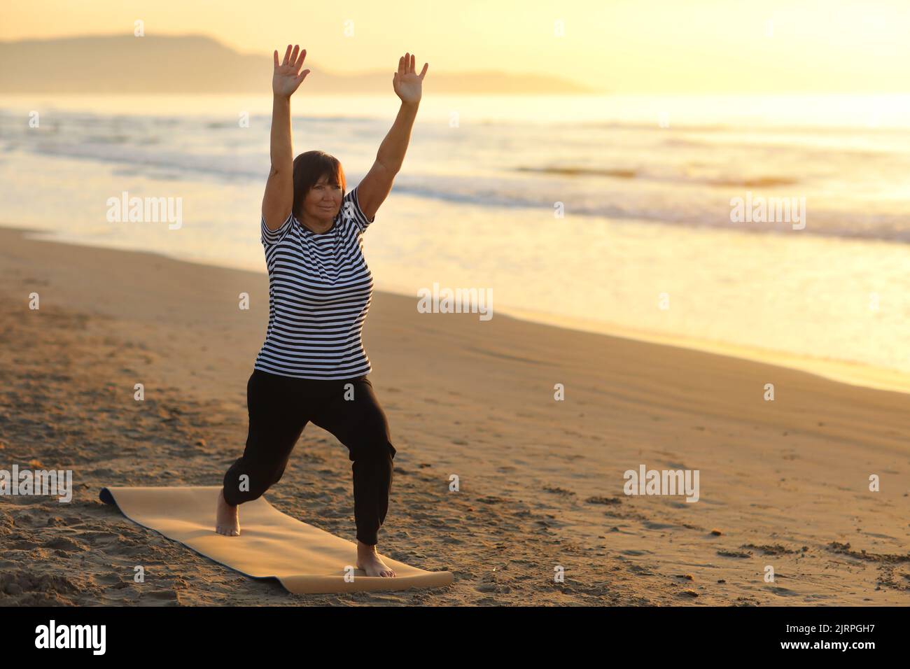Mature female takes care of body and does yoga by the sea outside on ...