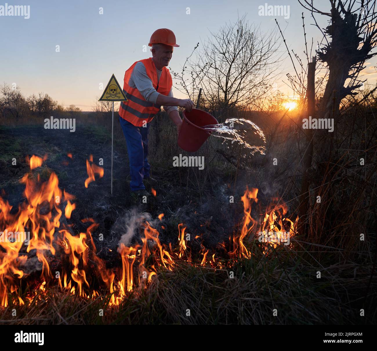Fireman ecologist extinguishing fire in field in the evening. Male ...