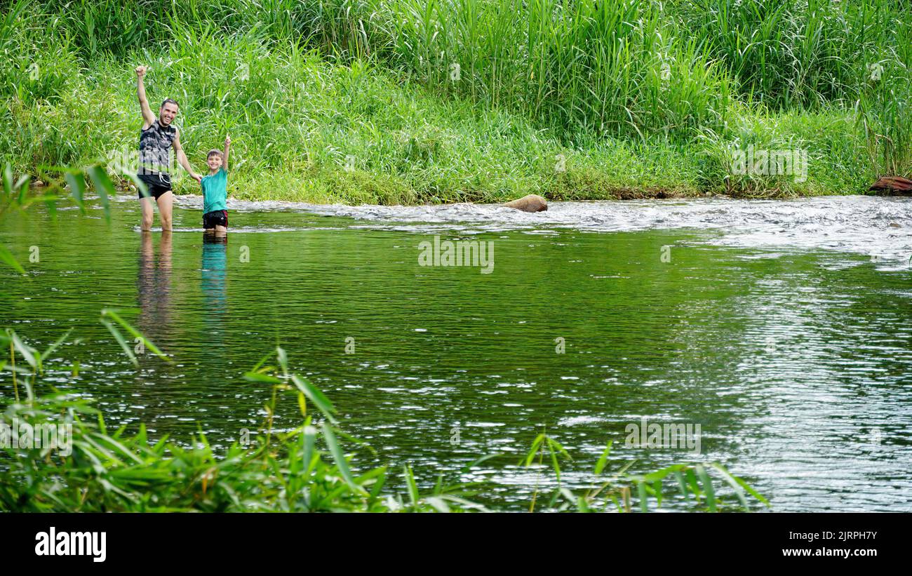 Father and son inside a river in the middle of the forest, waving in ...