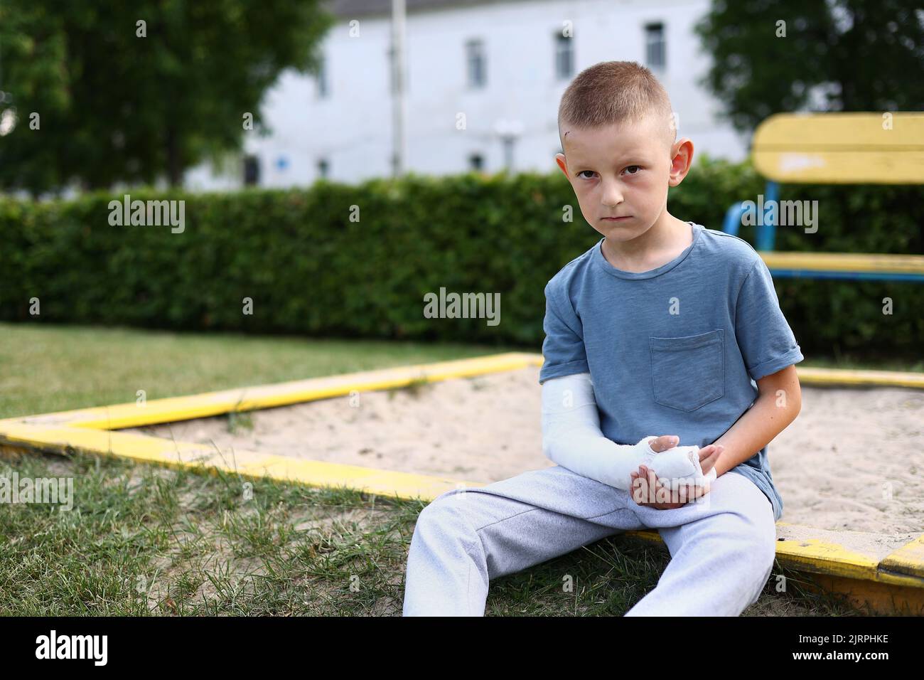 child caucasian with broken limb outdoors sits near the playground and ...